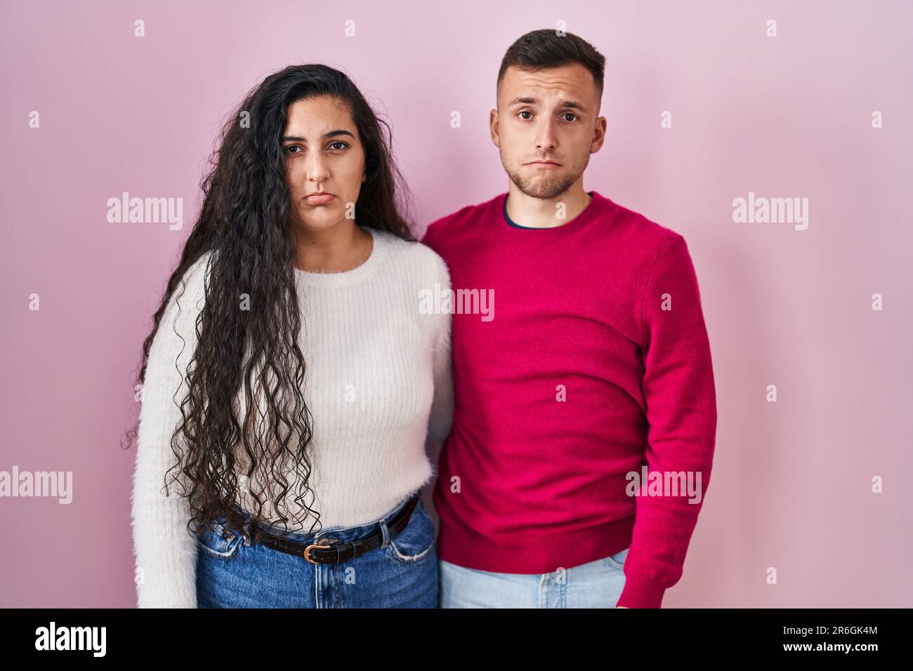 Young hispanic couple standing over pink background depressed and worry ...
