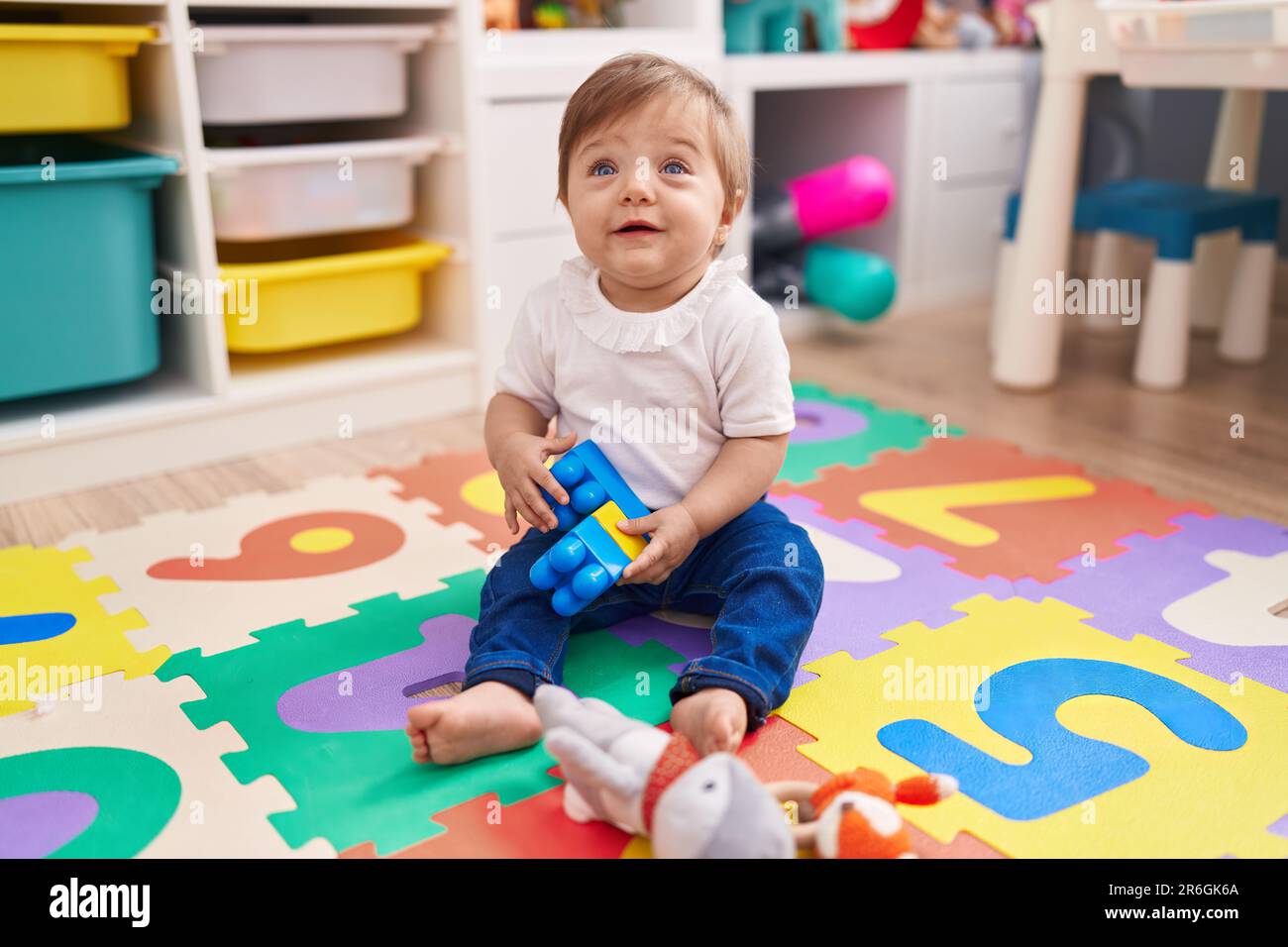 Adorable hispanic baby sitting on floor holding construction blocks at ...