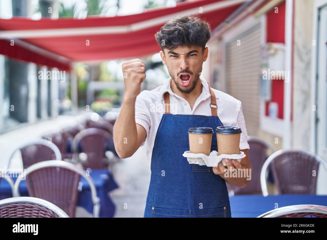 Arab man with beard wearing waiter apron at restaurant terrace annoyed ...