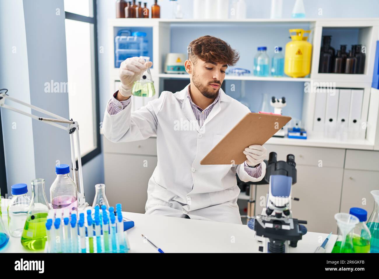 Young arab man scientist measuring liquid reading report at laboratory Stock Photo - Alamy
