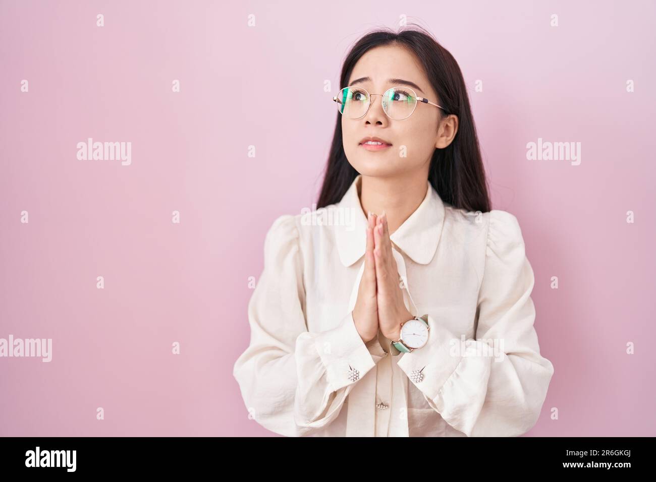 Young chinese woman standing over pink background begging and praying ...