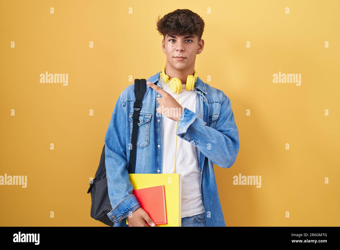 Hispanic teenager wearing student backpack and holding books pointing ...
