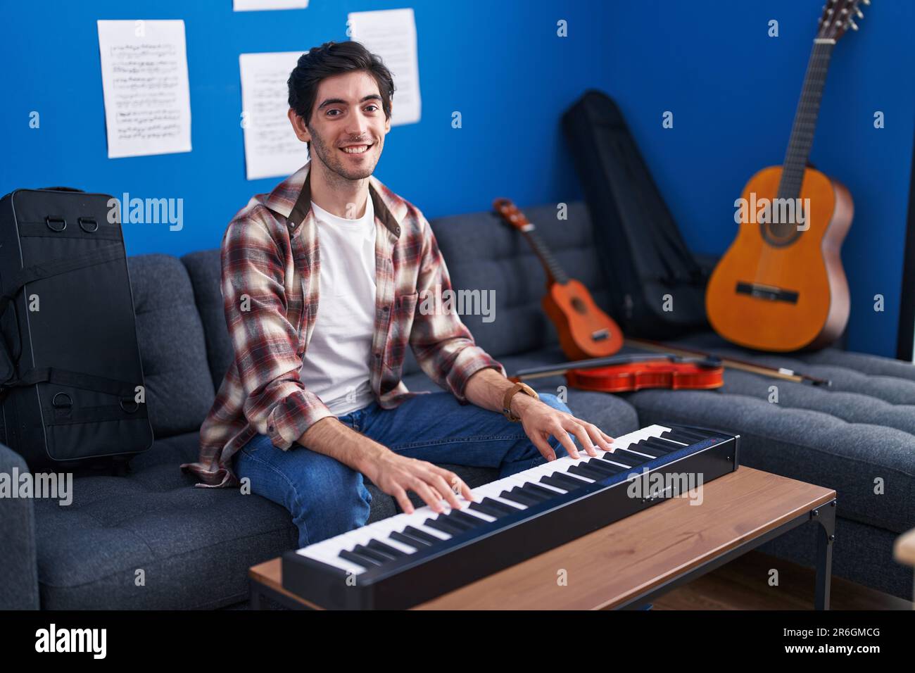 Young hispanic man playing piano at music studio smiling with a happy ...