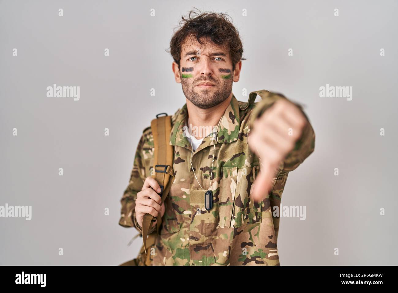 Hispanic young man wearing camouflage army uniform looking unhappy and ...