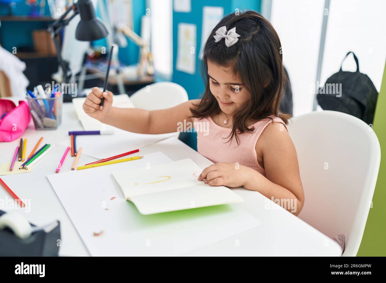 Adorable hispanic girl student writing on notebook at classroom Stock ...