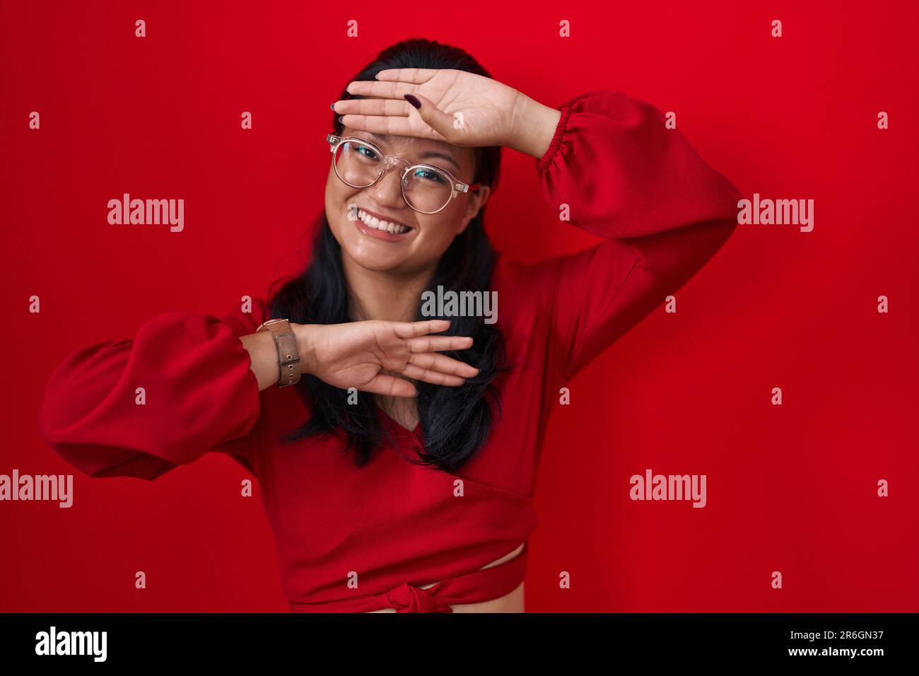 Asian young woman standing over red background smiling cheerful playing ...