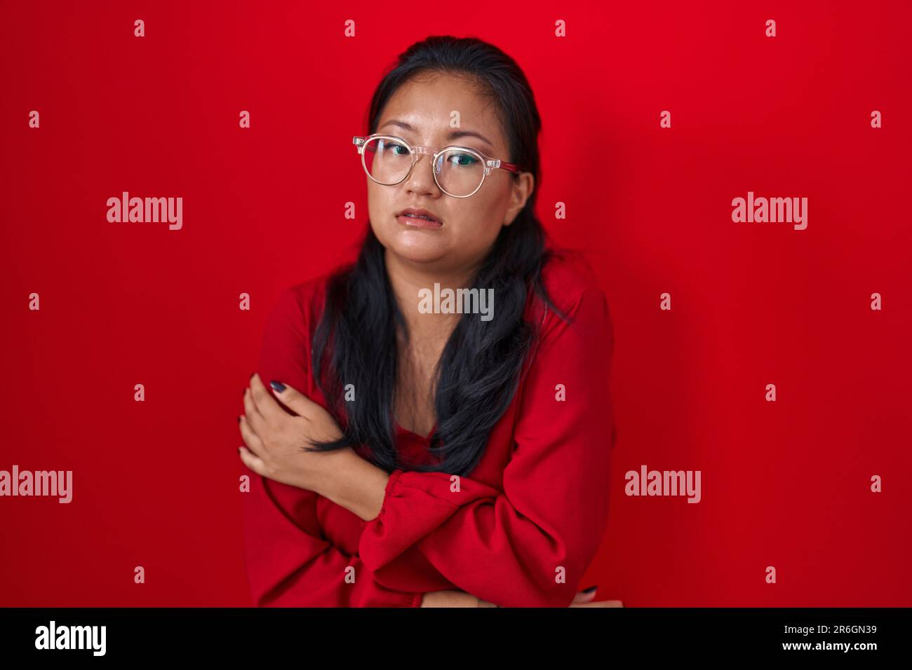 Asian young woman standing over red background shaking and freezing for ...