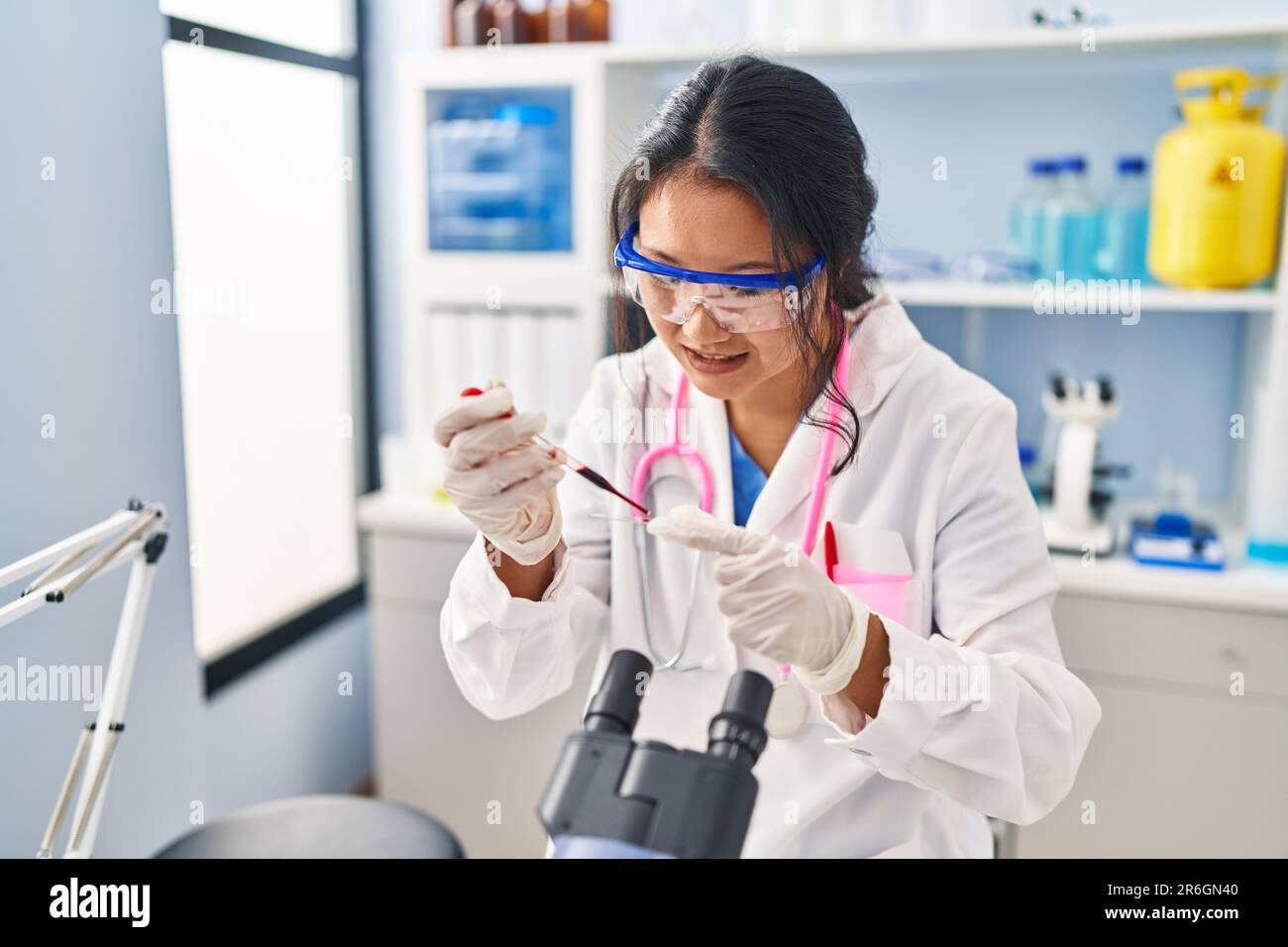Young chinese woman wearing scientist uniform analysing blood at ...