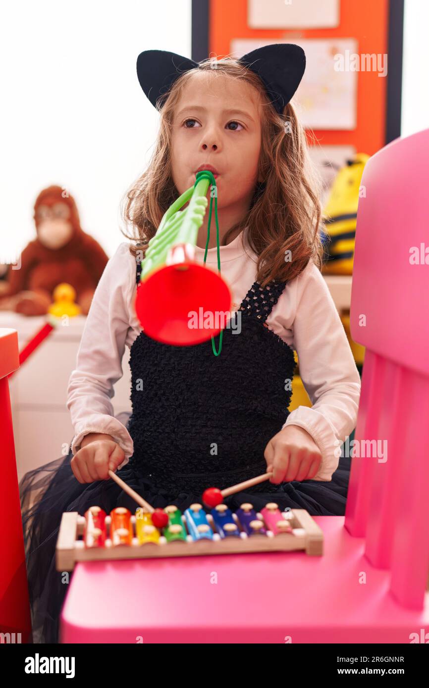 Adorable hispanic girl playing xylophone and trumpet at kindergarten ...