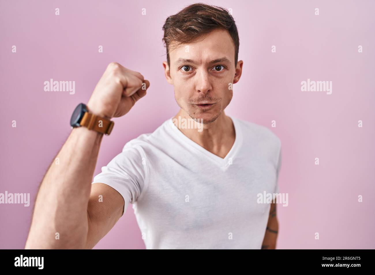 Caucasian man standing over pink background angry and mad raising fist ...