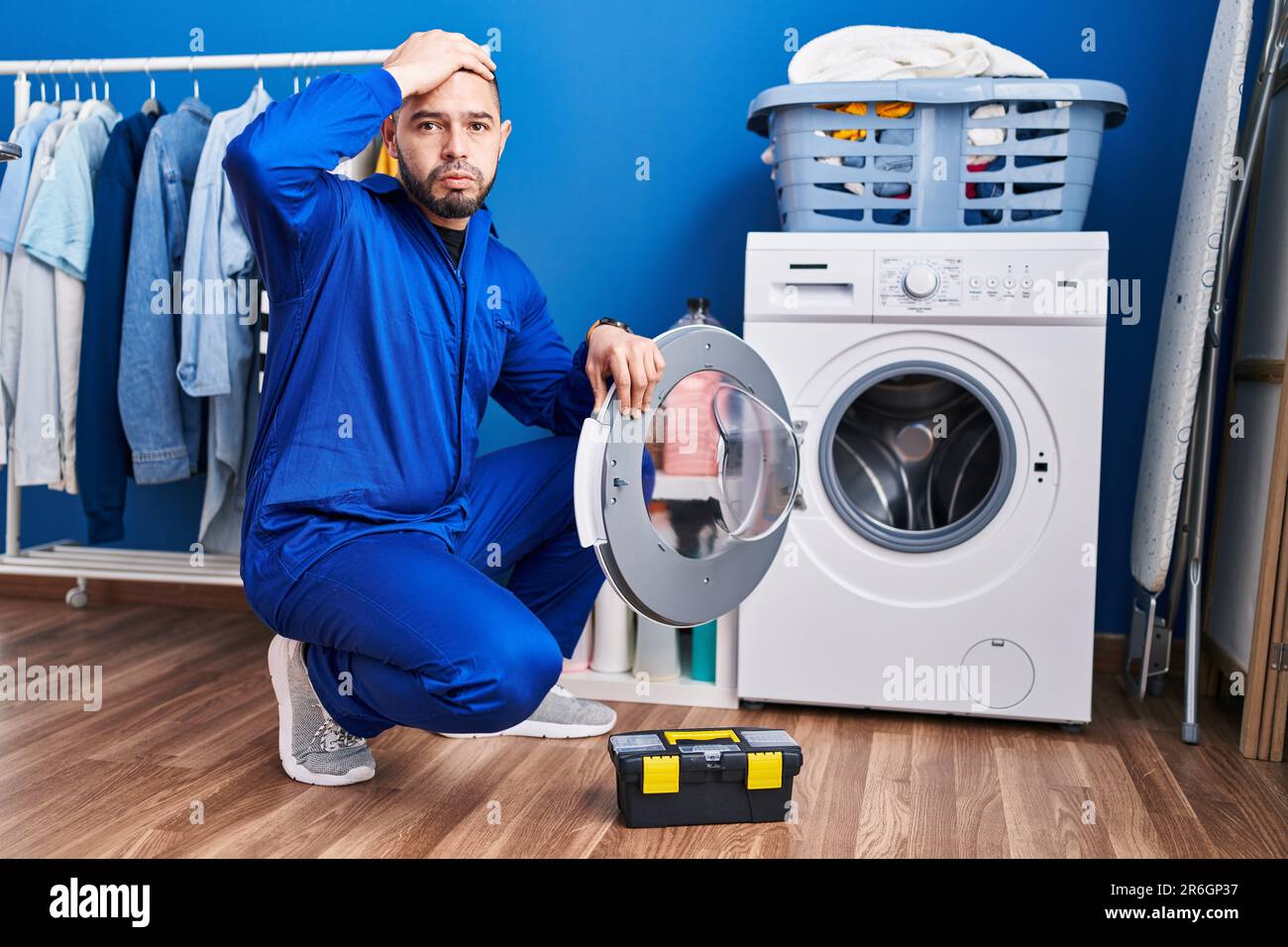 Hispanic repairman working on washing machine stressed and frustrated ...
