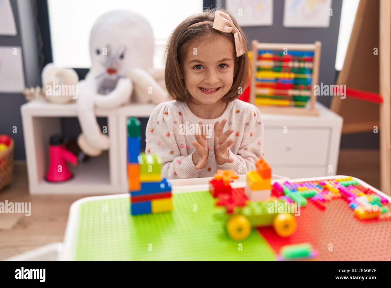 Adorable hispanic girl playing with construction blocks clapping hands ...