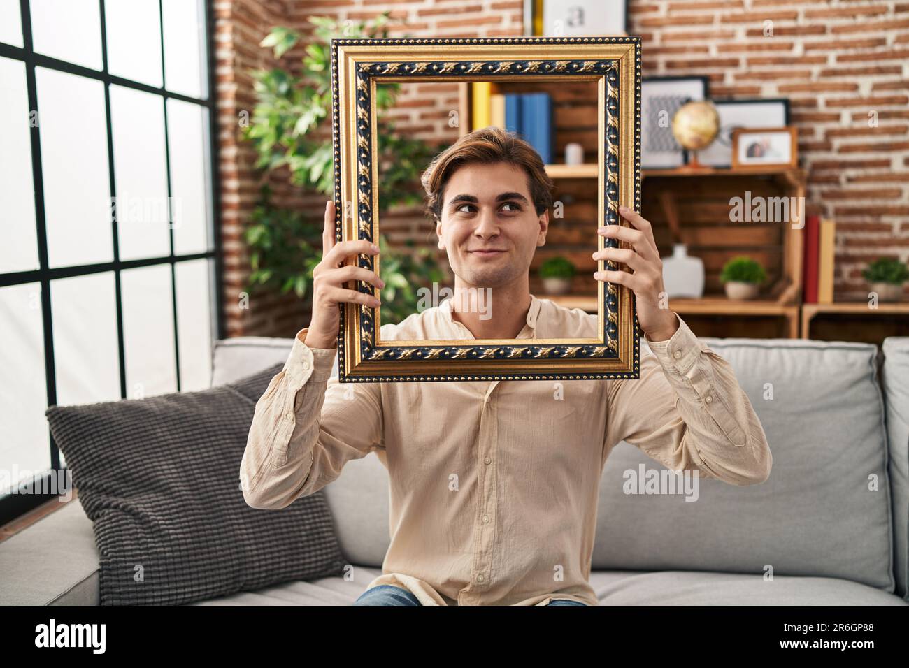 Young man holding empty frame smiling looking to the side and staring ...