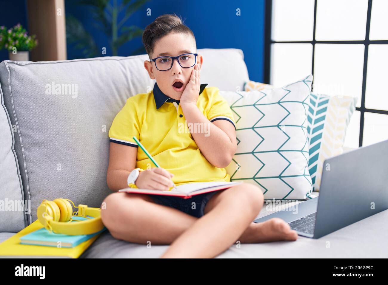 Young hispanic kid doing homework sitting on the sofa afraid and ...