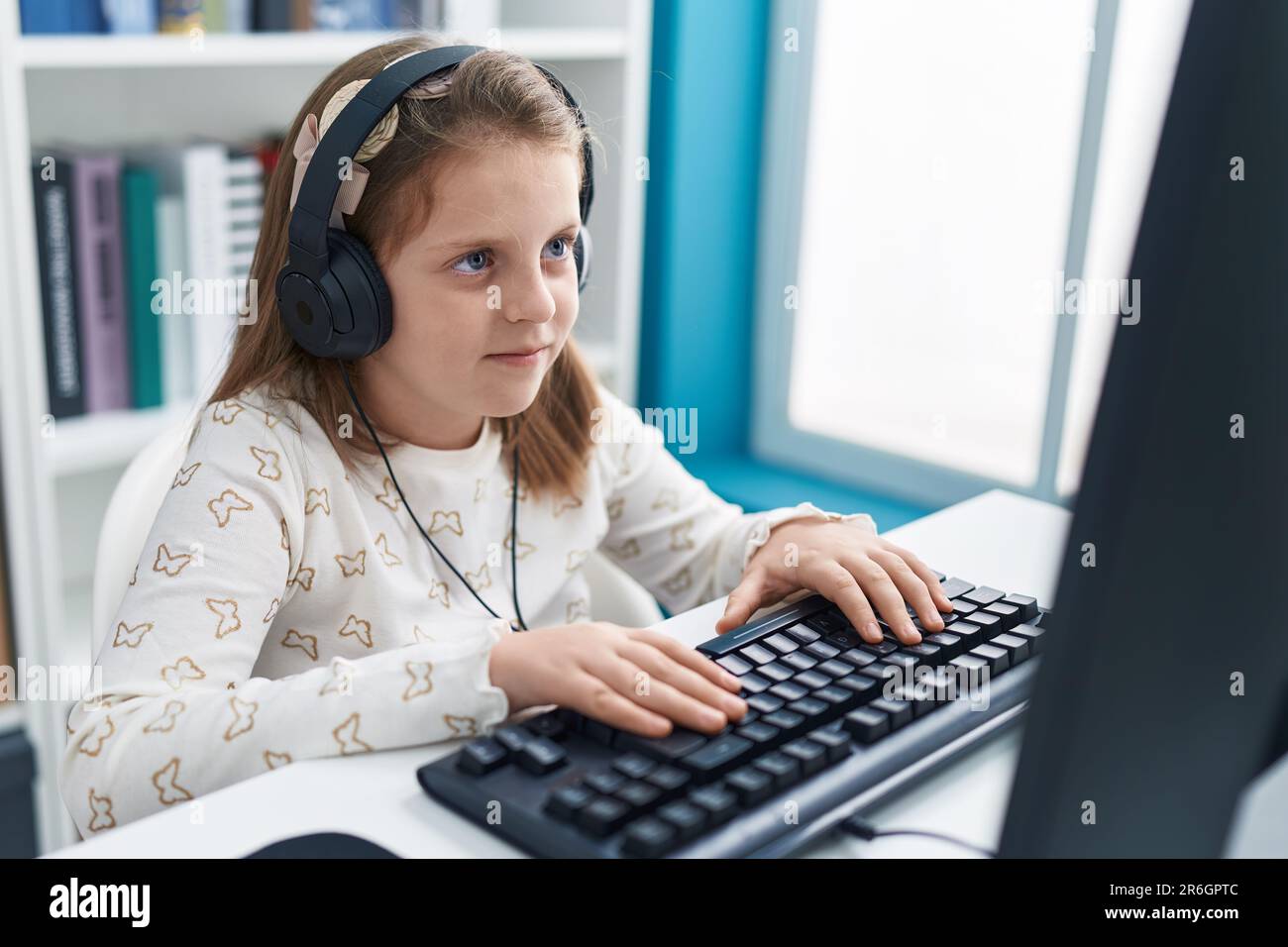 Adorable blonde girl student using computer and headphones studying at ...