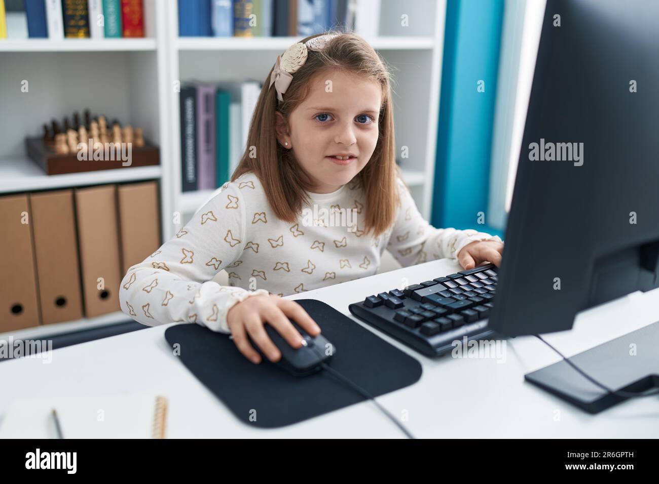 Adorable blonde girl student using computer sitting on table at ...