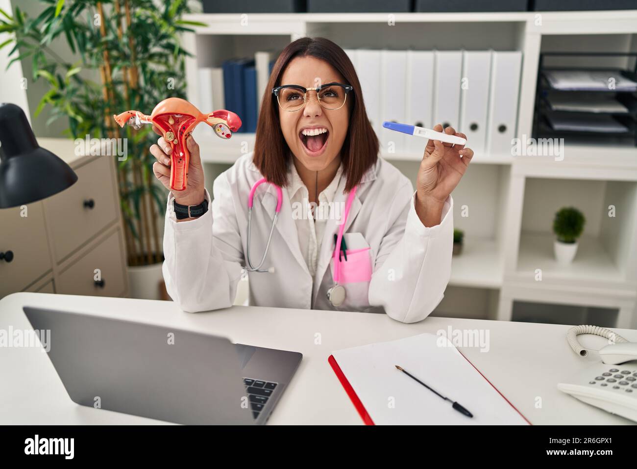Young hispanic doctor woman holding anatomical model of female genital ...