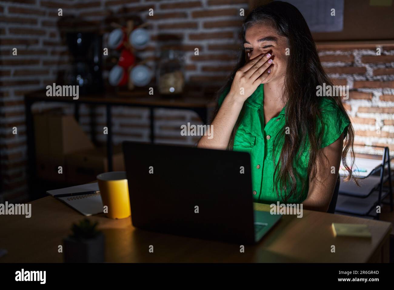 Young teenager girl working at the office at night smelling something ...