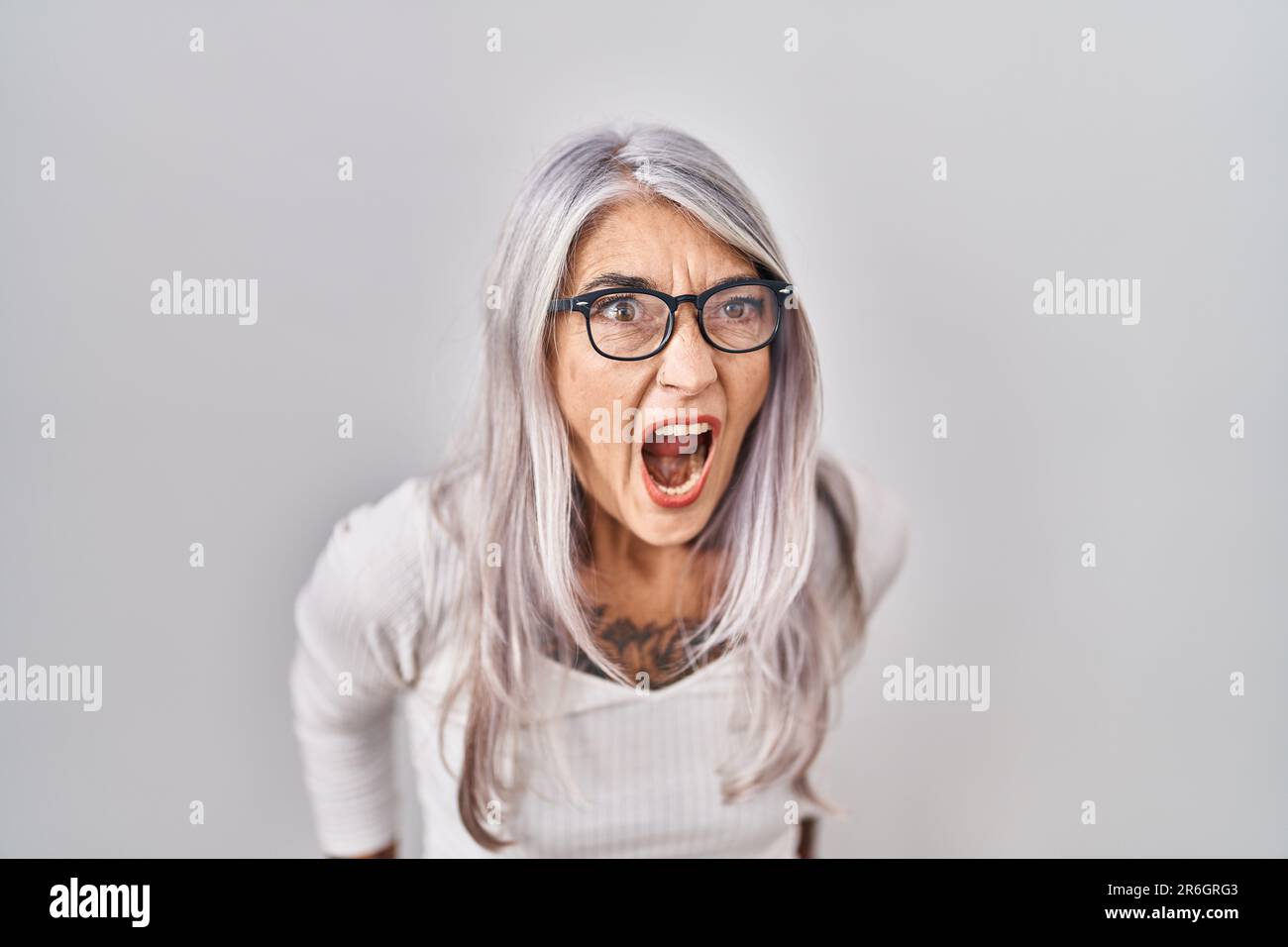 Middle age woman with grey hair standing over white background angry ...