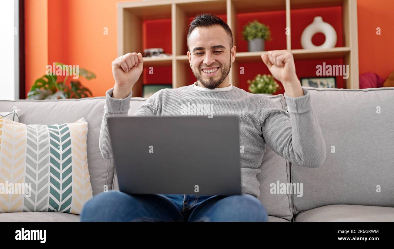 Hispanic man using laptop celebrating sitting on the sofa at home Stock ...