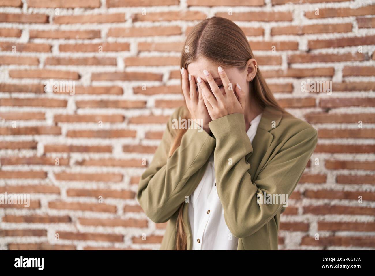 Young caucasian woman standing over bricks wall background with sad ...