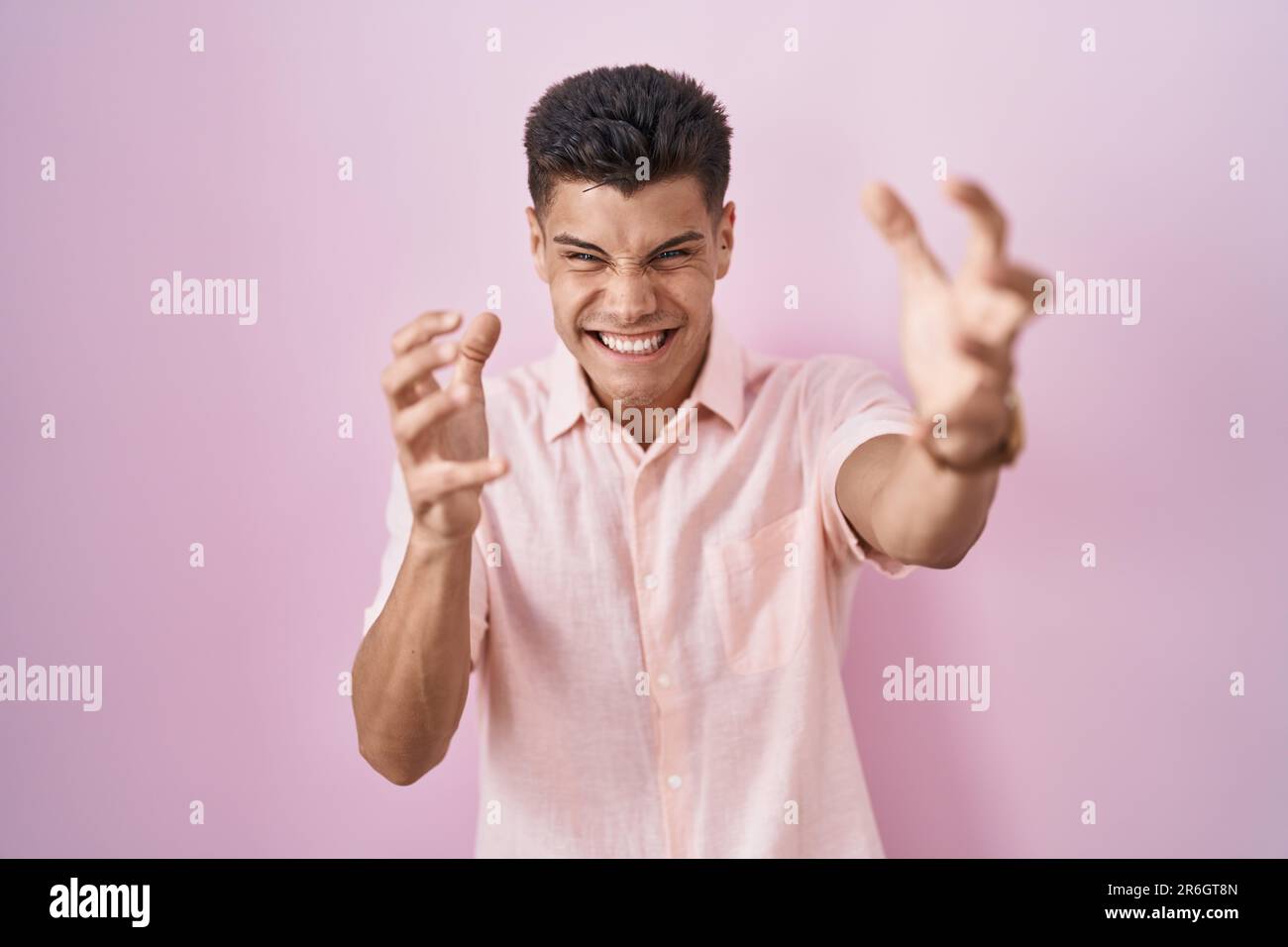 Young hispanic man standing over pink background shouting frustrated ...