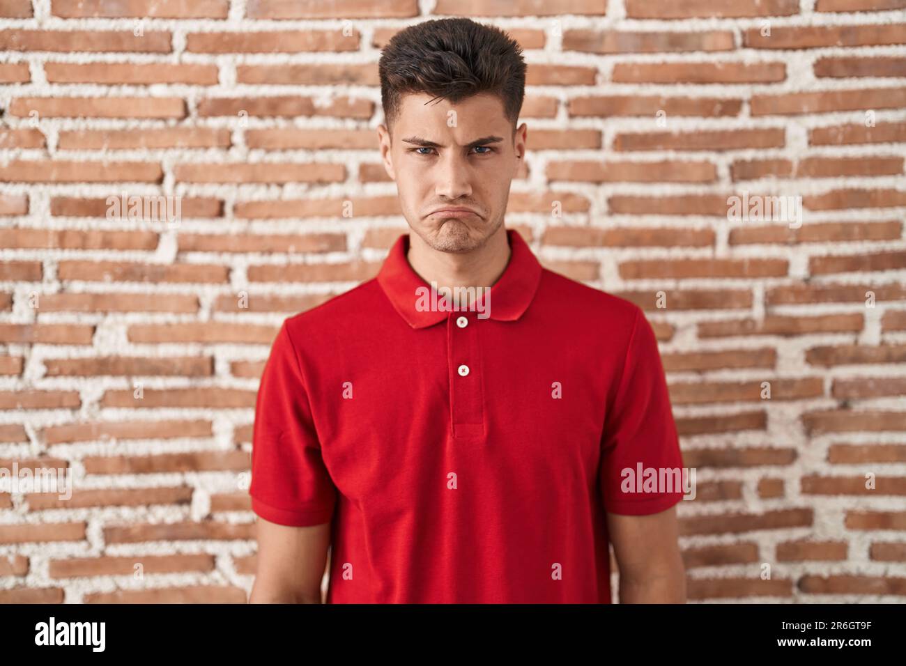 Young hispanic man standing over bricks wall depressed and worry for ...