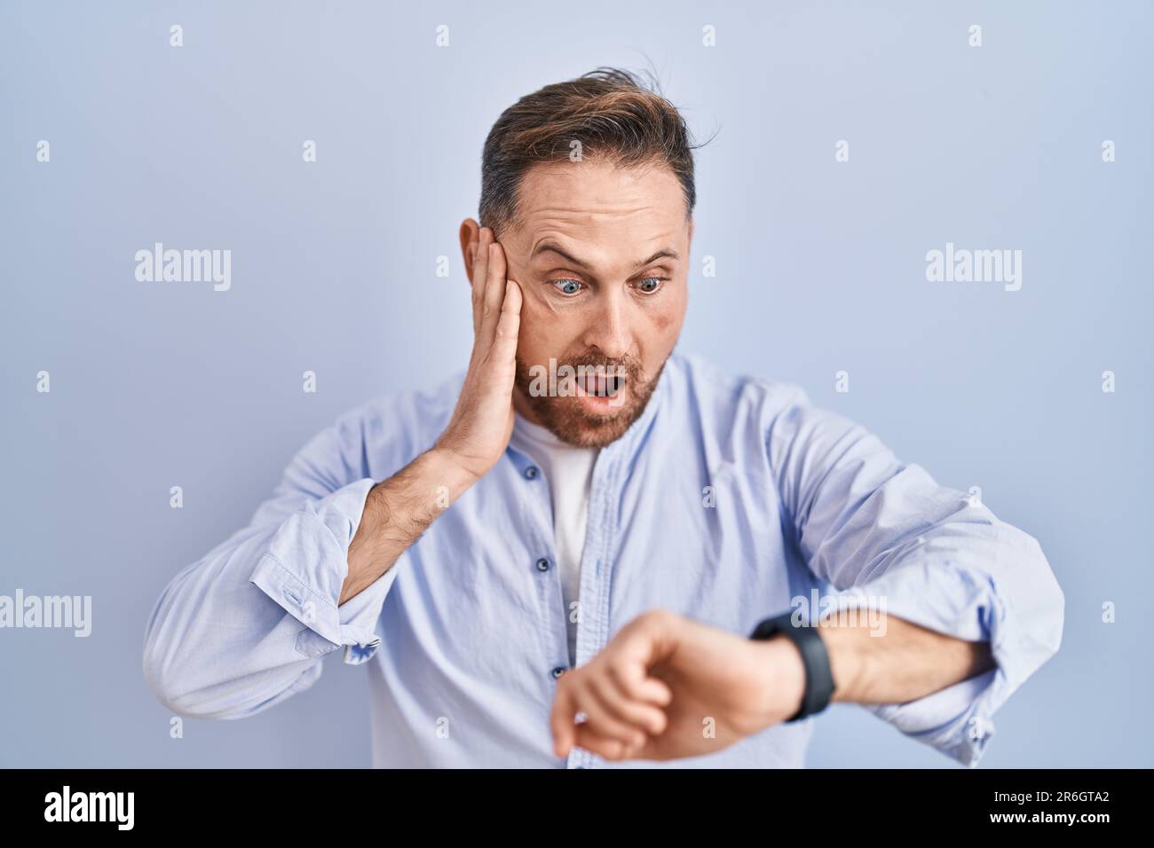 Middle age caucasian man standing over blue background looking at the ...