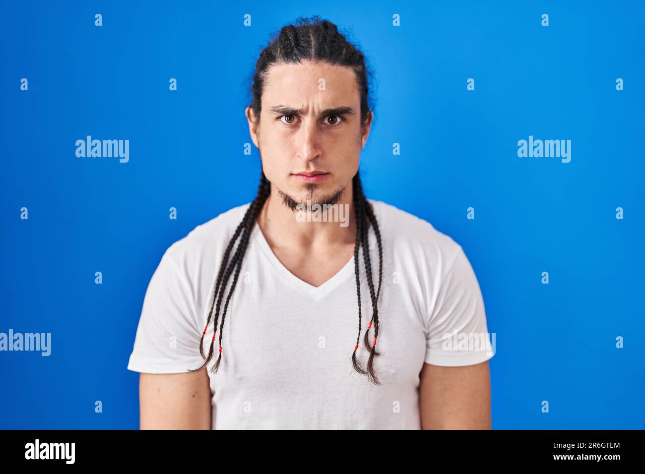 Hispanic man with long hair standing over blue background skeptic and ...