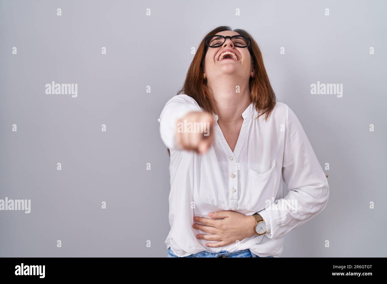 Brunette woman standing over white isolated background laughing at you ...
