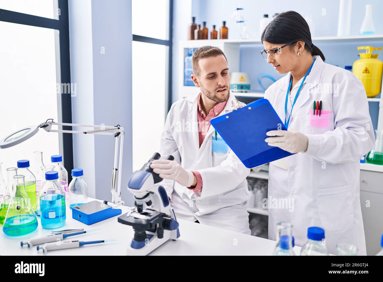 Man and woman wearing scientists uniform using microscope at laboratory ...