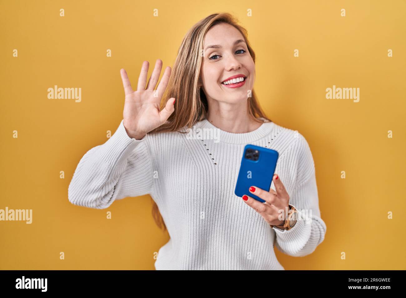 Young blonde woman using smartphone typing message waiving saying hello ...