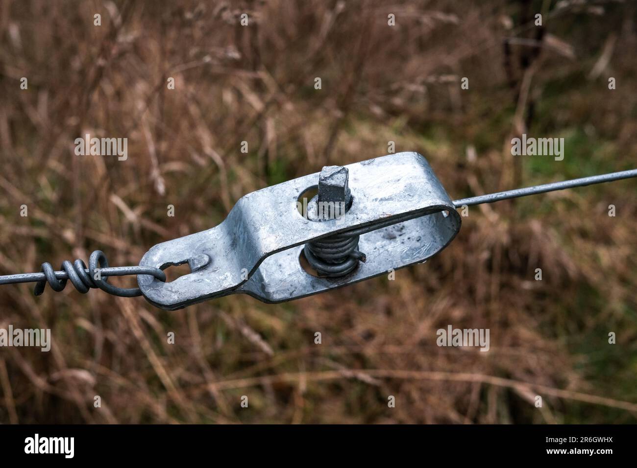 A metal clamp attached to a barbed wire fence with electrical wires ...