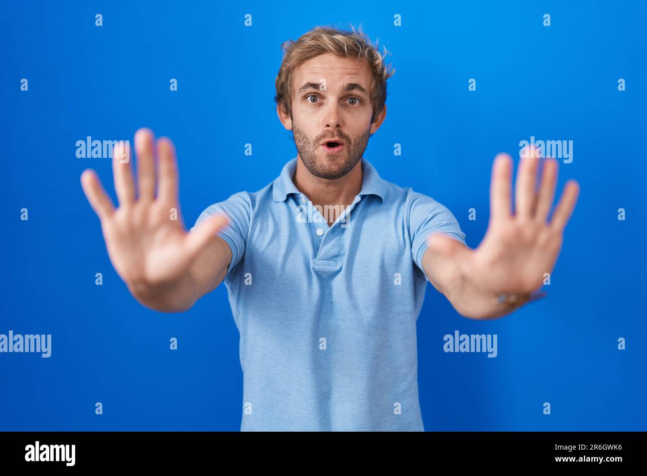 Caucasian man standing over blue background doing stop gesture with ...