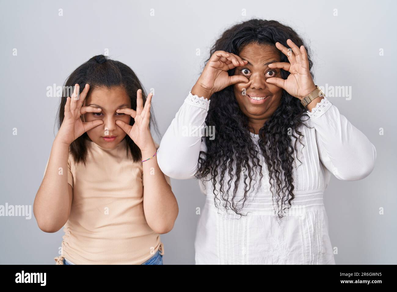 Mother and young daughter standing over white background trying to open ...