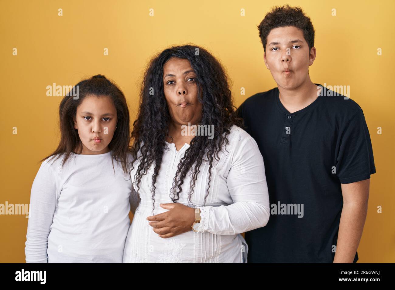 Family of mother, daughter and son standing over yellow background ...