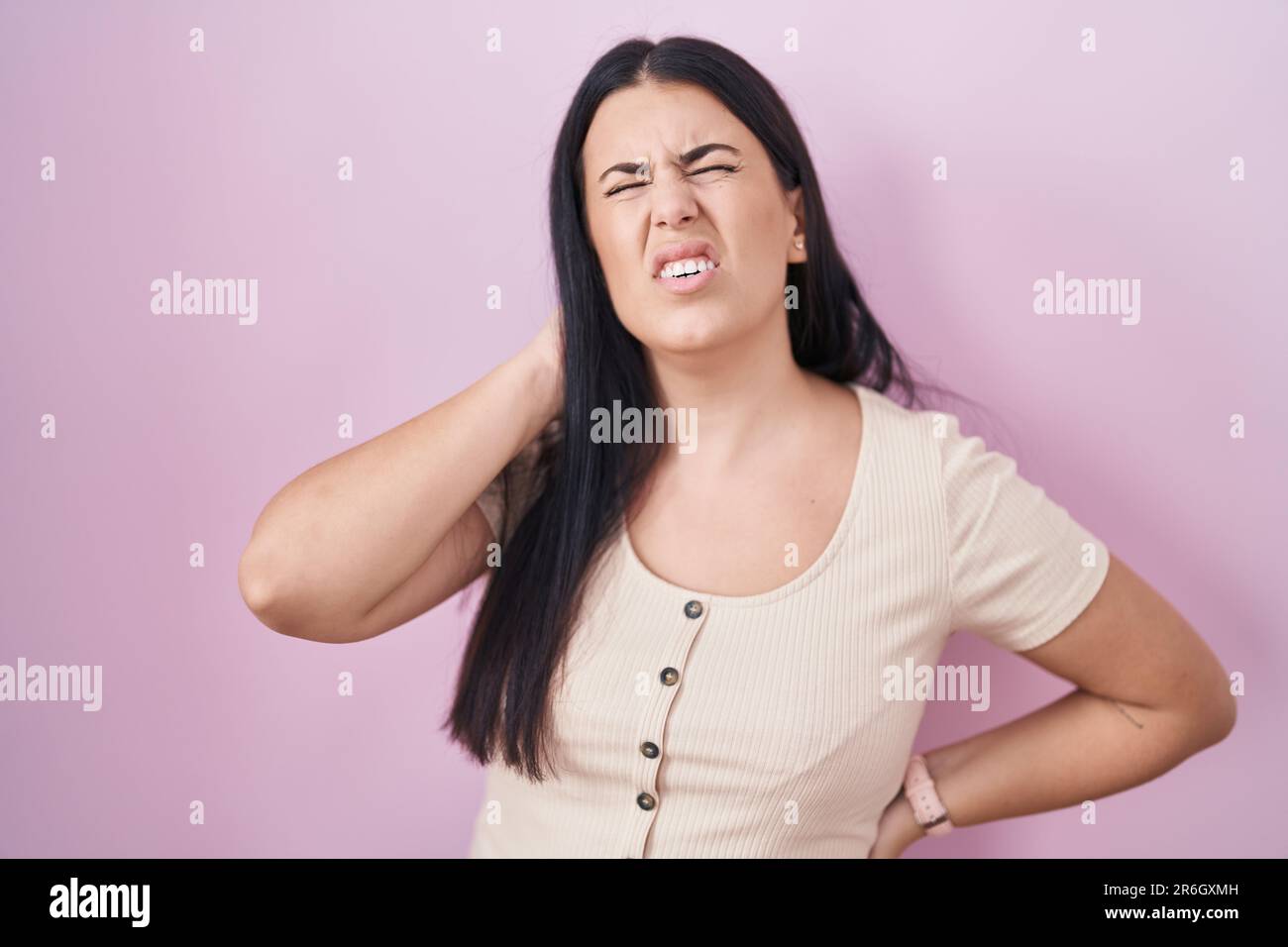 Young hispanic woman standing over pink background suffering of neck ...