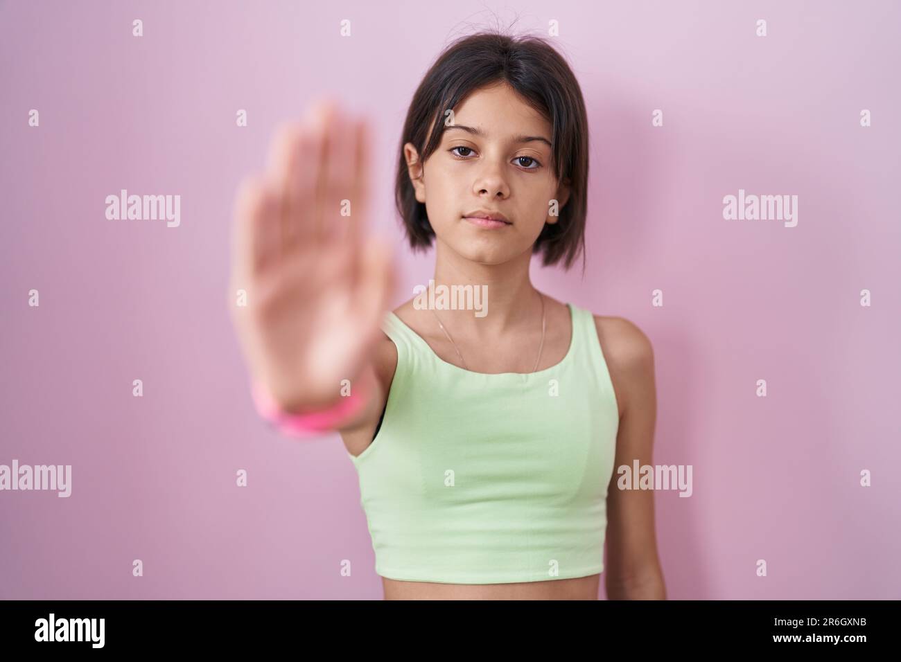 Young girl standing over pink background doing stop sing with palm of ...