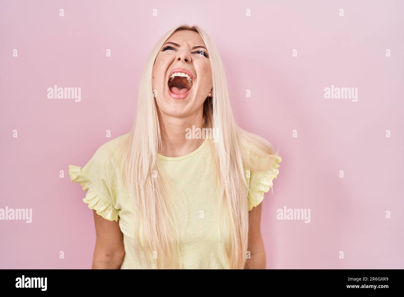 Caucasian woman standing over pink background angry and mad screaming ...