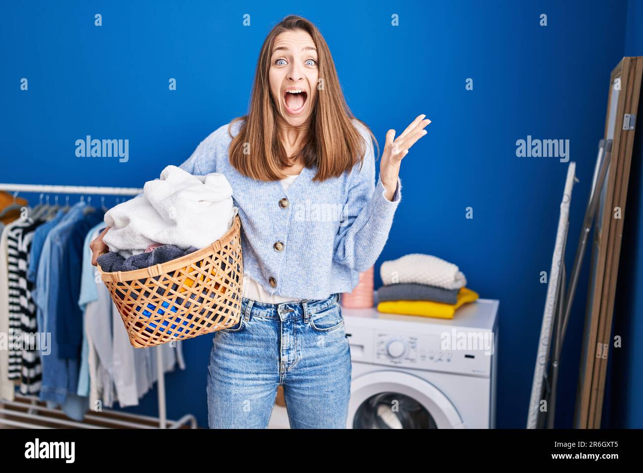 Young woman holding laundry basket celebrating victory with happy smile ...