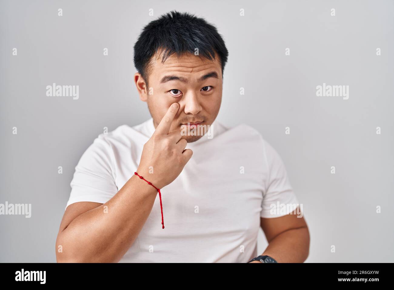 Young chinese man standing over white background pointing to the eye ...