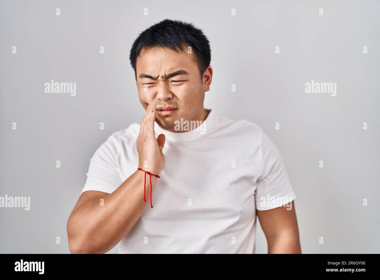 Young chinese man standing over white background touching mouth with ...