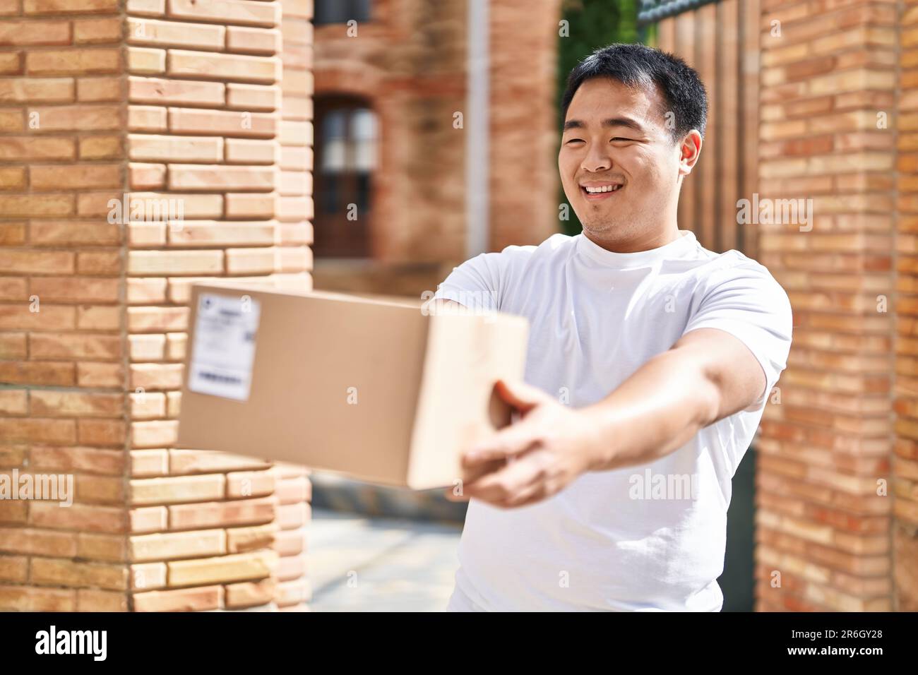 Young chinese man courier holding package at street Stock Photo - Alamy