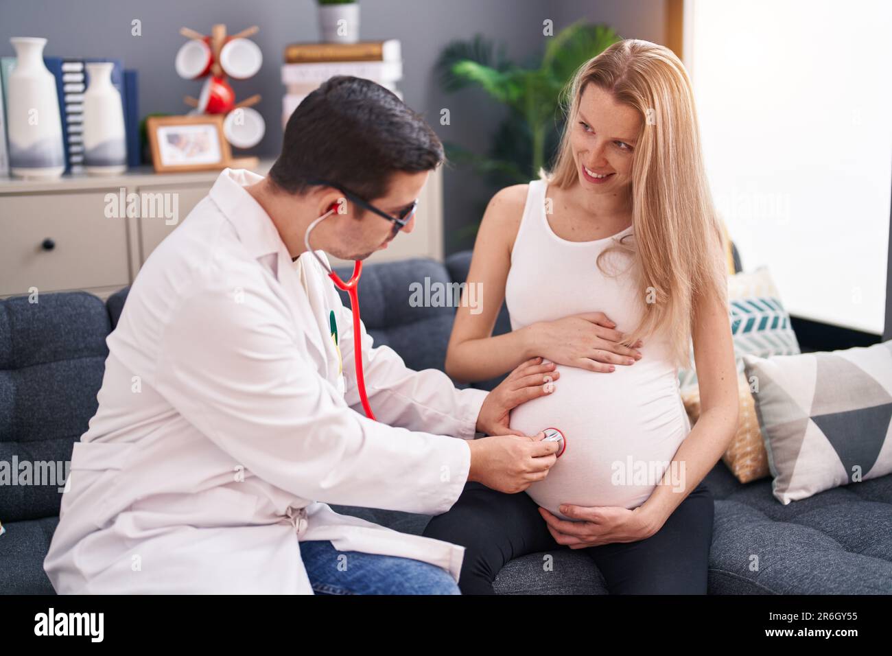 Man and woman doctor and pregnant patient auscultating baby at home ...