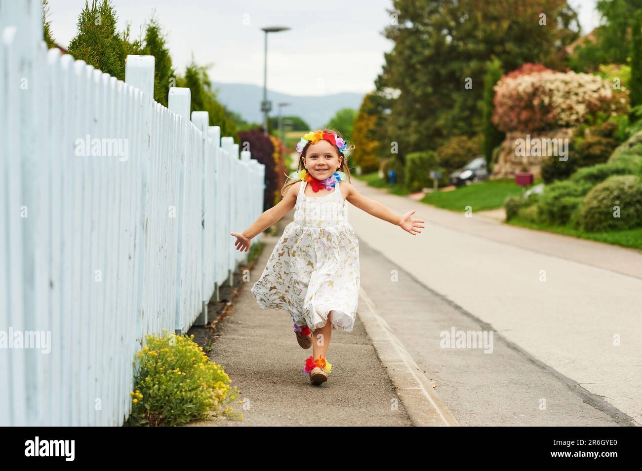 Little girl running down the street, wearing white dress, arms wide ...