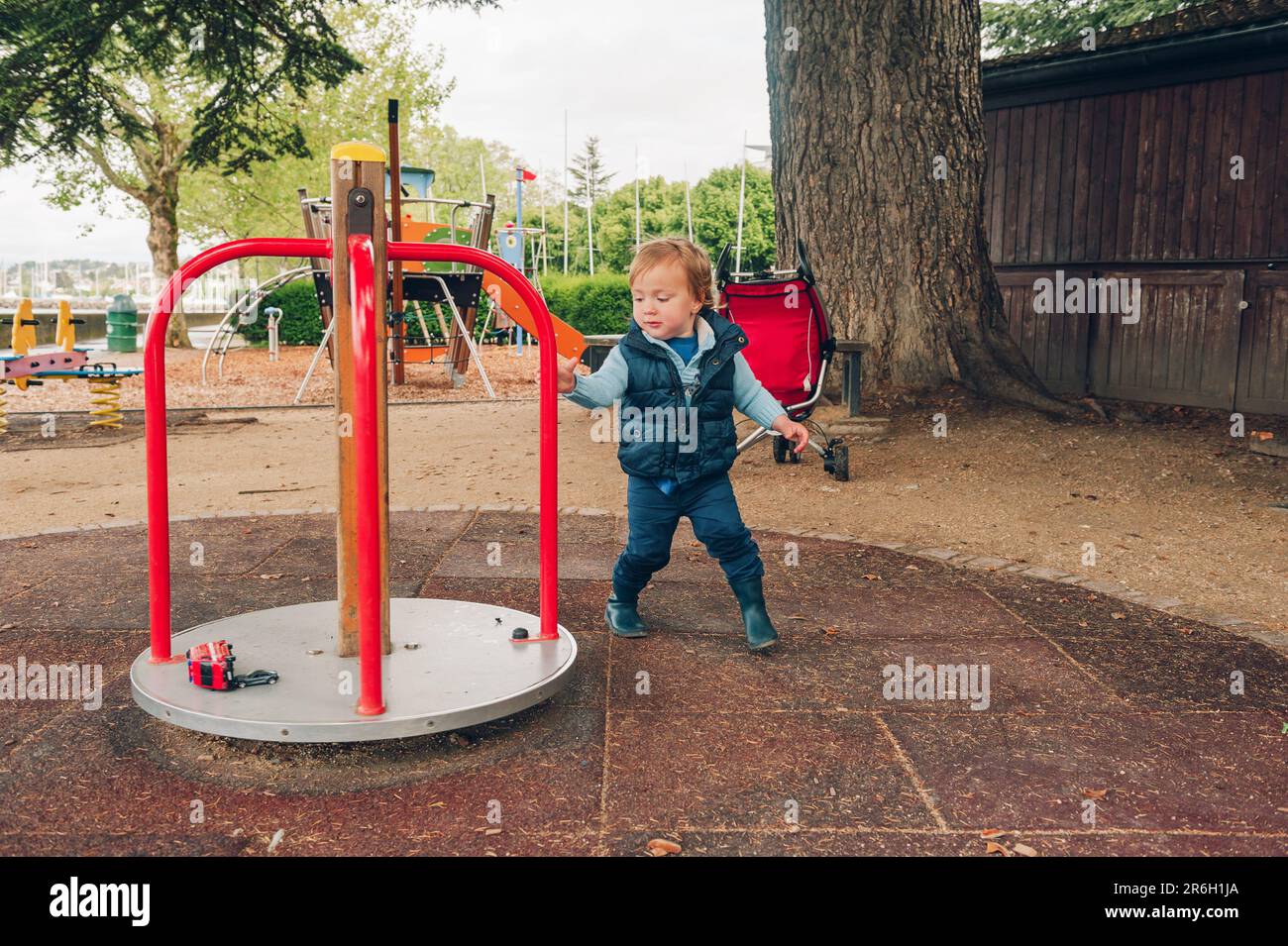 Funny toddler boy having fun on playground, rides toy car on merry-go ...