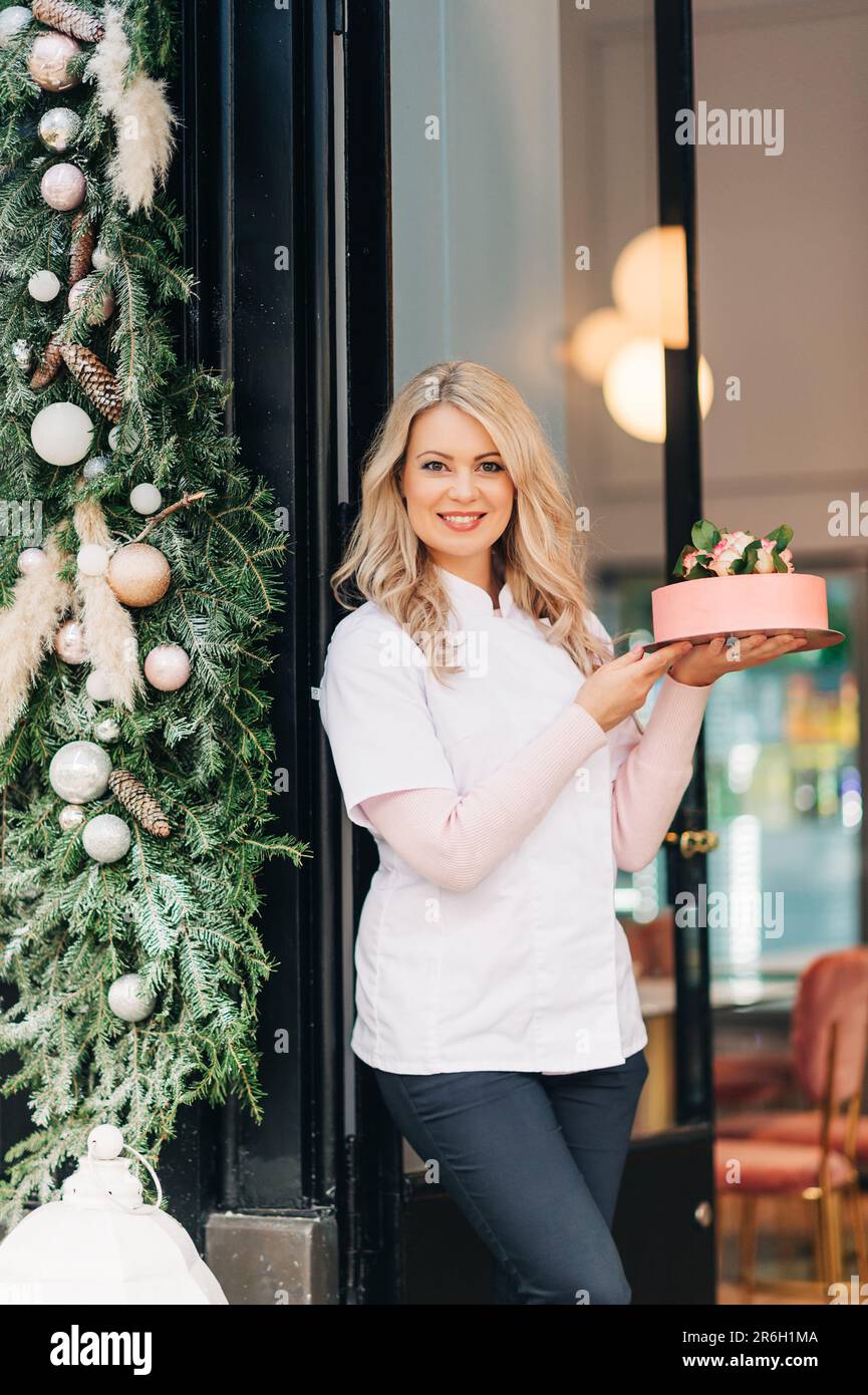 Portrait of cheerful baker woman standing next to facade of Tea Room ...