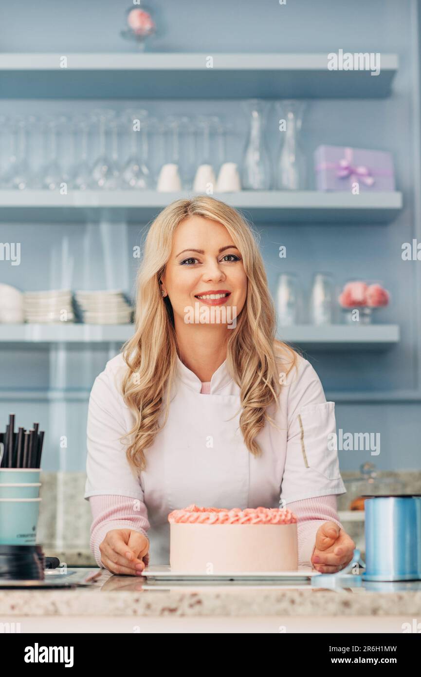 Portrait of cheerful baker woman cut pink cake, standing behind the ...