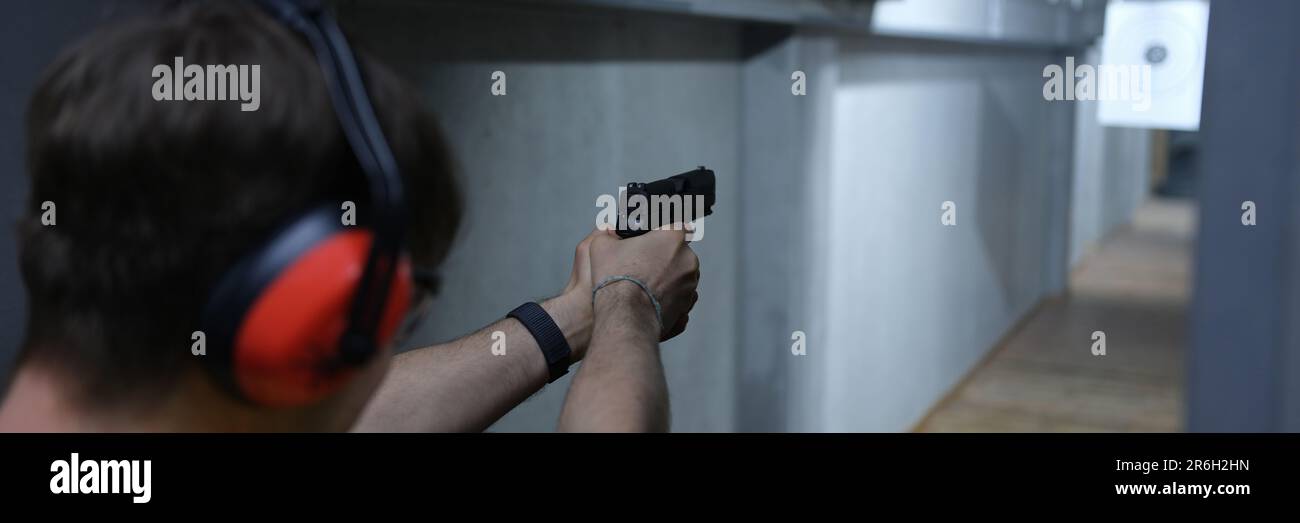 Man shooter in tactical headphones aiming pistol at target in shooting ...