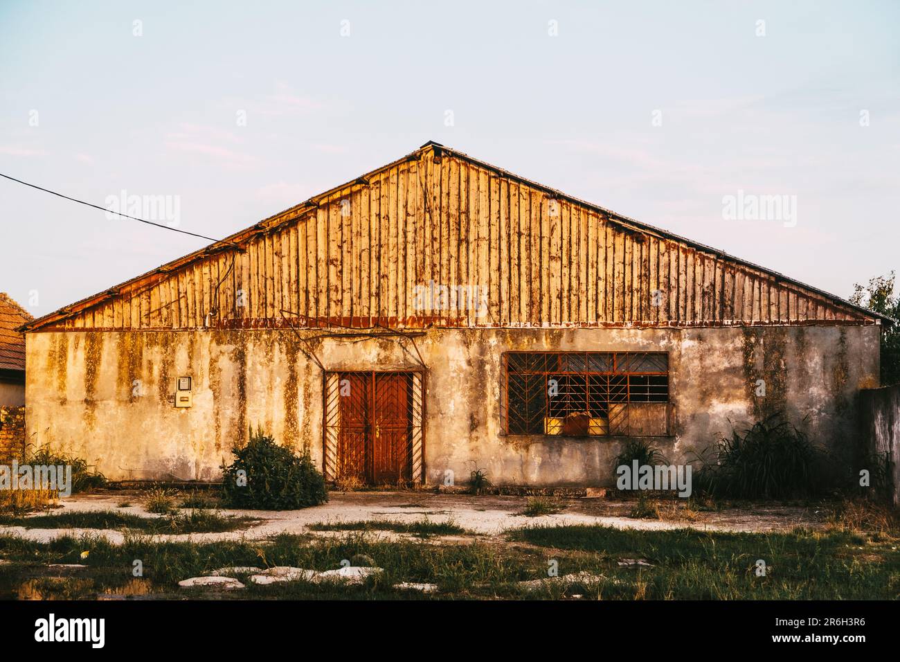 A rural building standing in a grassy field, with a clear blue sky ...
